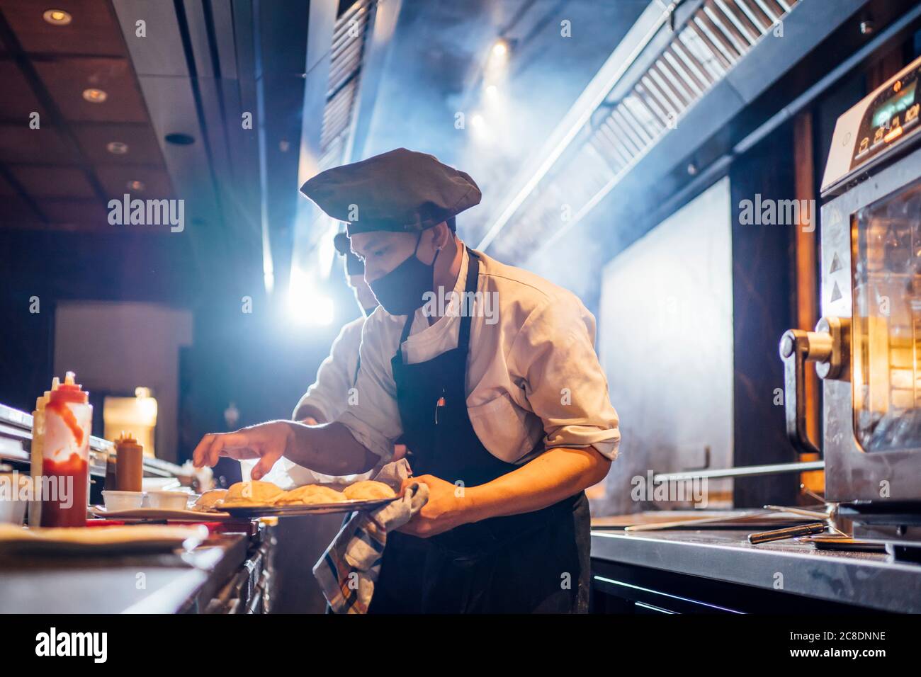 Chef wearing protective face mask preparing a dish in restaurant ...