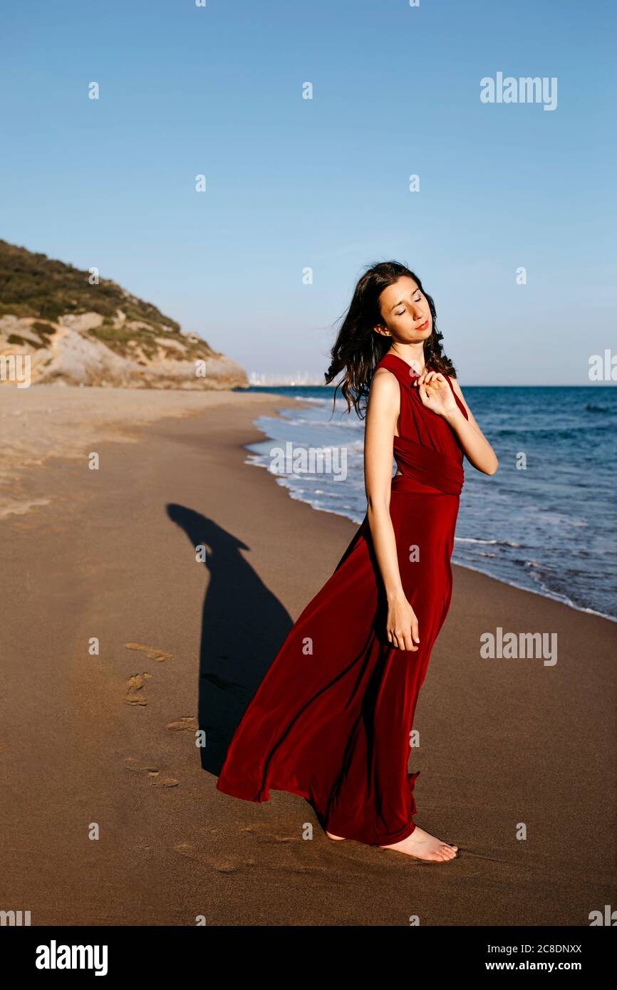 Delicate woman in red dress standing at the sea, feeling the sun Stock ...