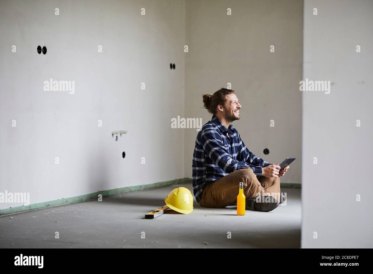 Happy worker on a construction site having a break sitting on the floor ...