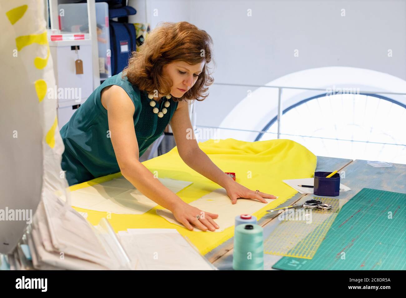 Female fashion designer adjusting yellow fabric at workbench in atelier ...