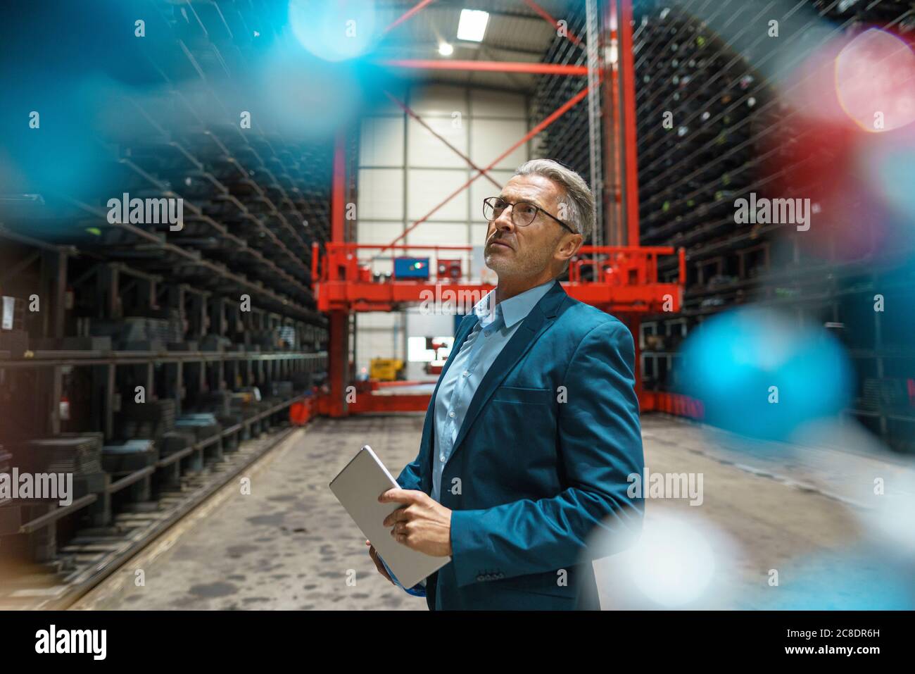 Mature businessman holding tablet in a high rack warehouse of a factory ...