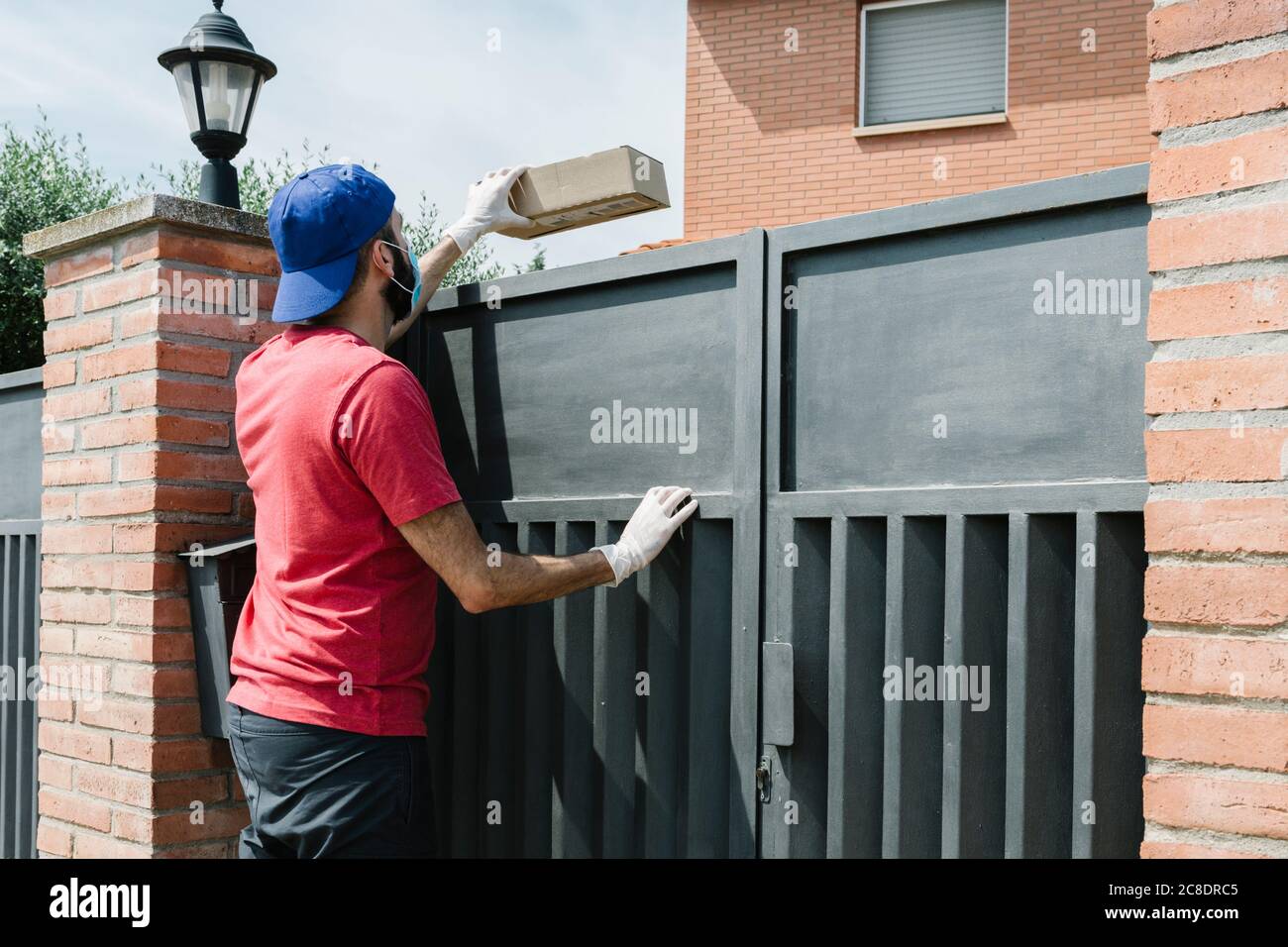 Male delivery person giving package from over gate of house Stock Photo ...