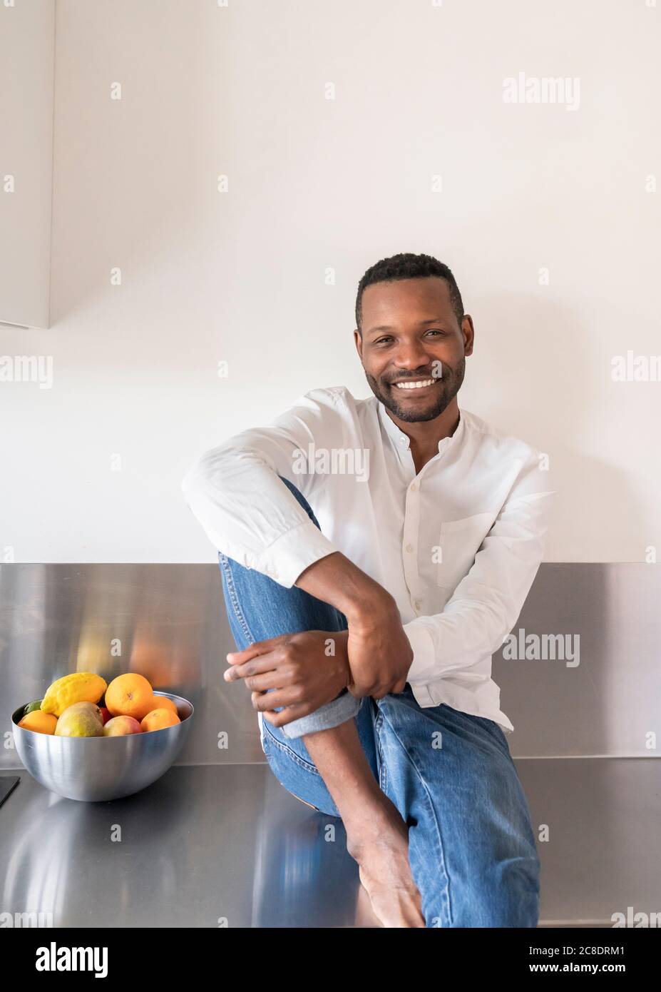 Portrait of smiling man sitting on kitchen counter at home Stock Photo ...