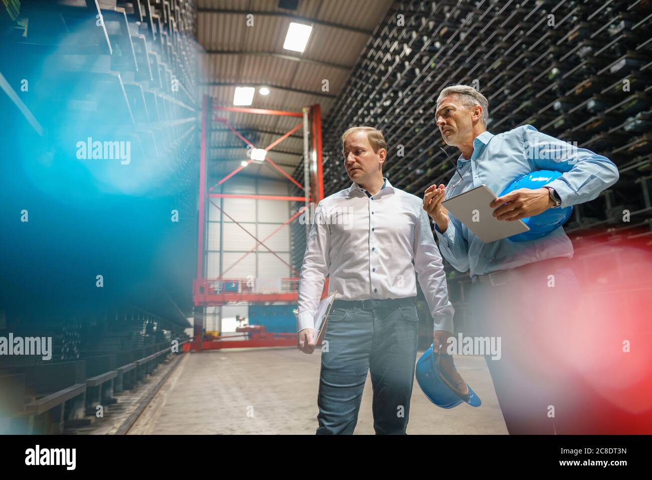 Two businessmen having a meeting in a high rack warehouse of a factory ...