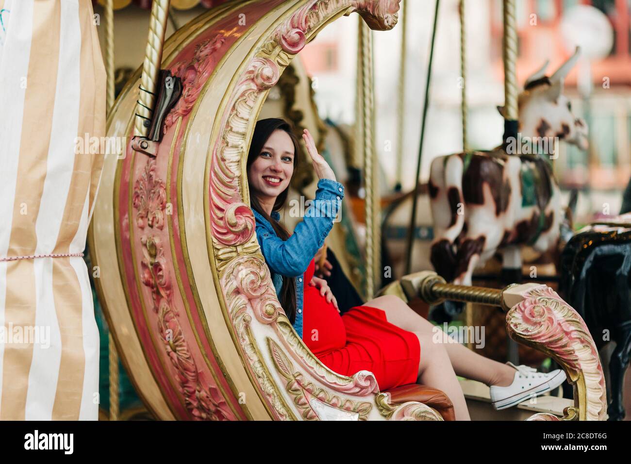 Happy pregnant woman waving while sitting on carousel at amusement park ...