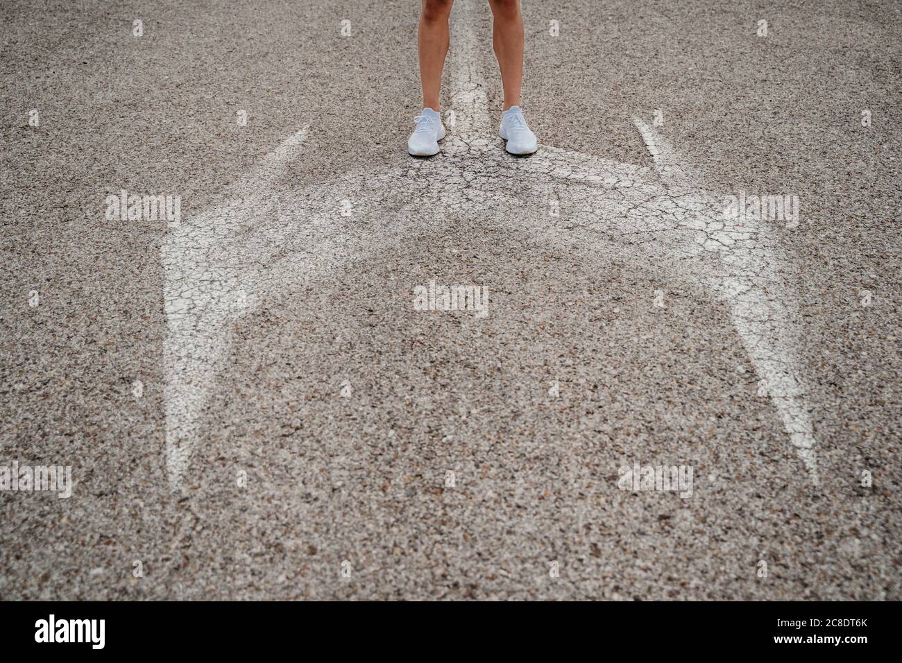 Male athlete standing at arrow signs on the road Stock Photo - Alamy