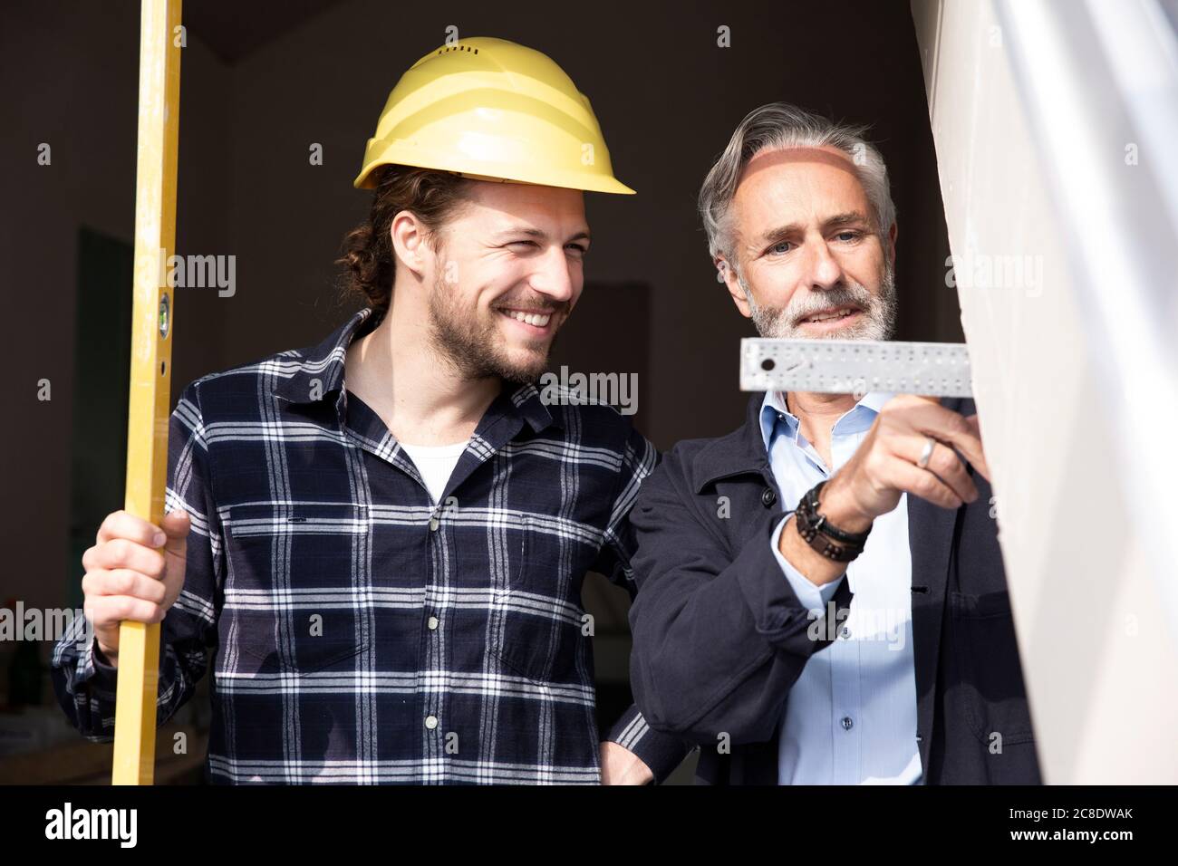 Smiling construction worker looking at measurement showing by architect ...