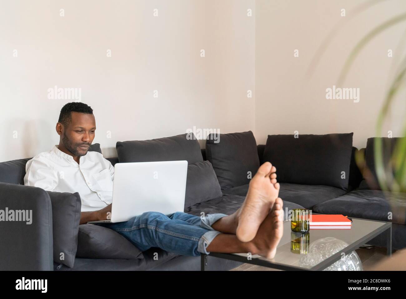 Portrait of man sitting on couch with feet up using laptop Stock Photo ...