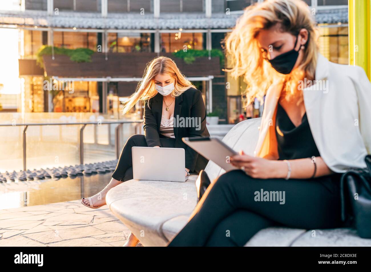 Female entrepreneurs wearing masks working over computers while sitting ...