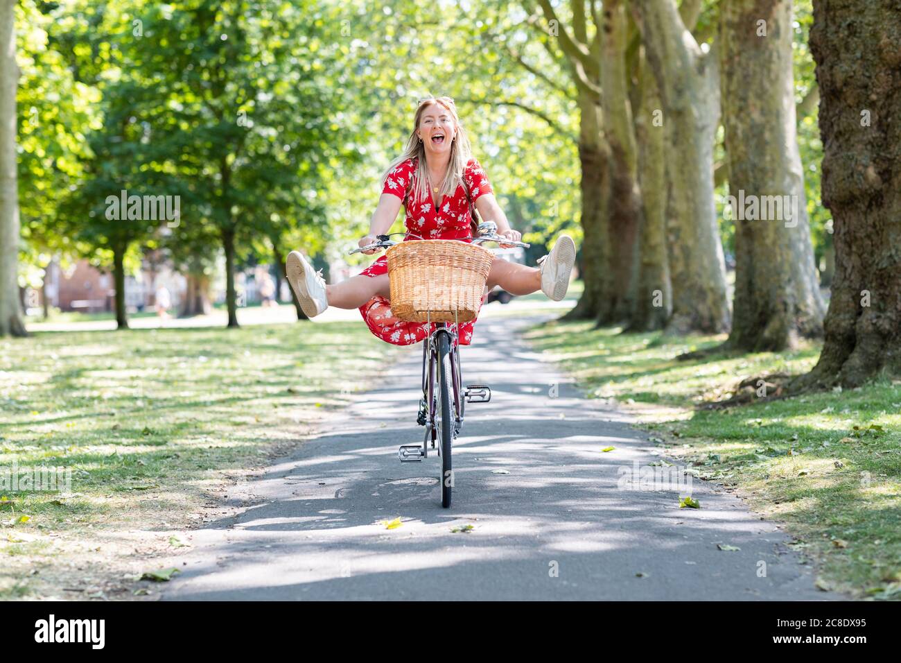 Cheerful woman with feet up riding bicycle on footpath at public park ...
