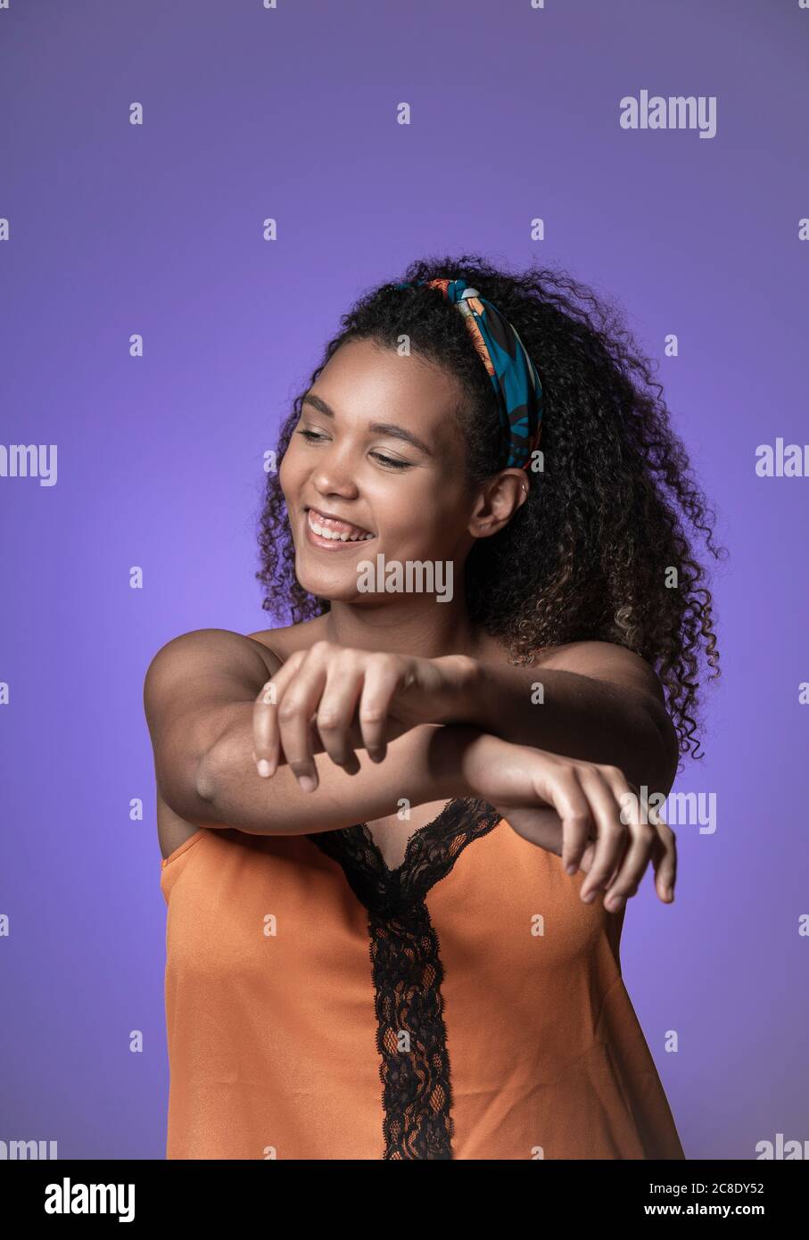 Cheerful young woman with curly hair dancing against purple background ...