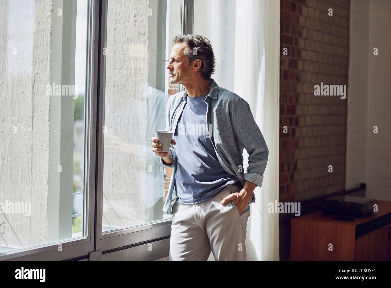 Senior man looking out of window in a loft flat Stock Photo - Alamy