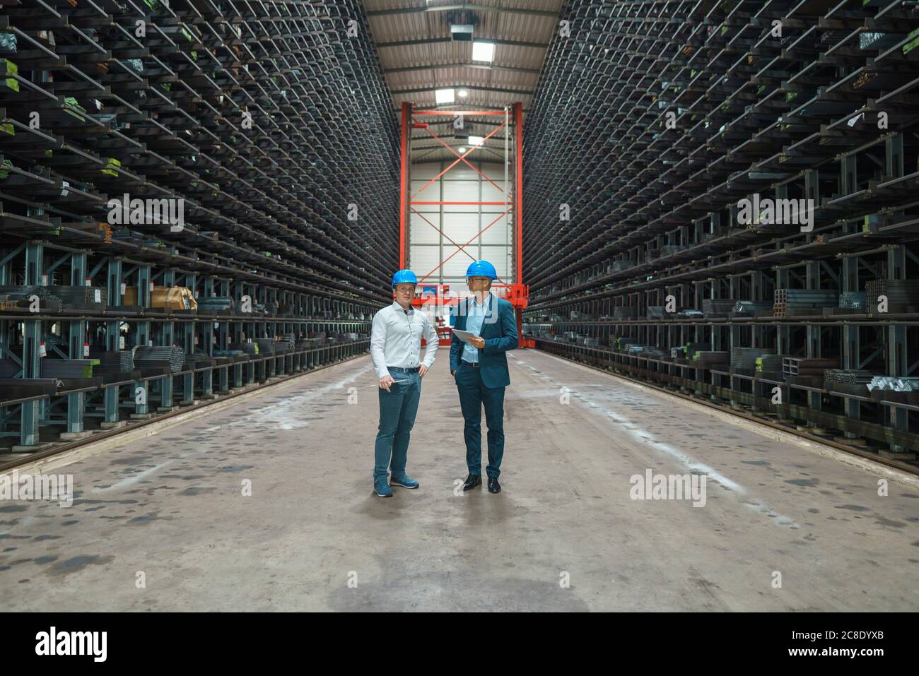 Two businessmen having a meeting in a high rack warehouse of a factory ...
