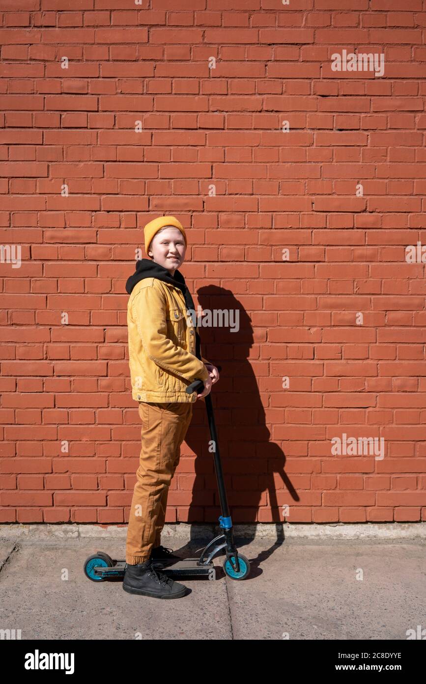 Boy standing with push scooter on sidewalk against brick wall Stock ...