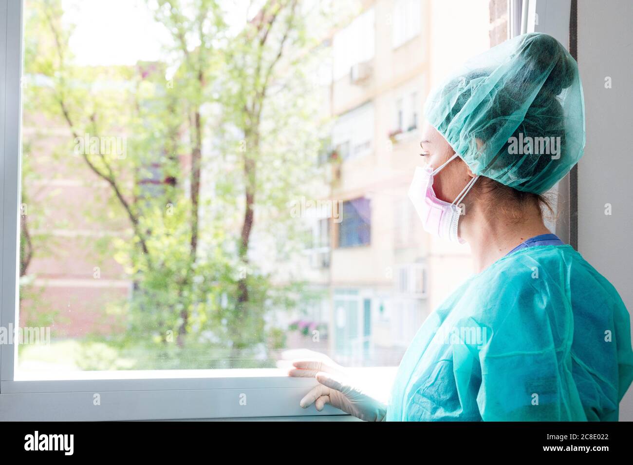 Female nurse wearing protective workwear looking through window in ...