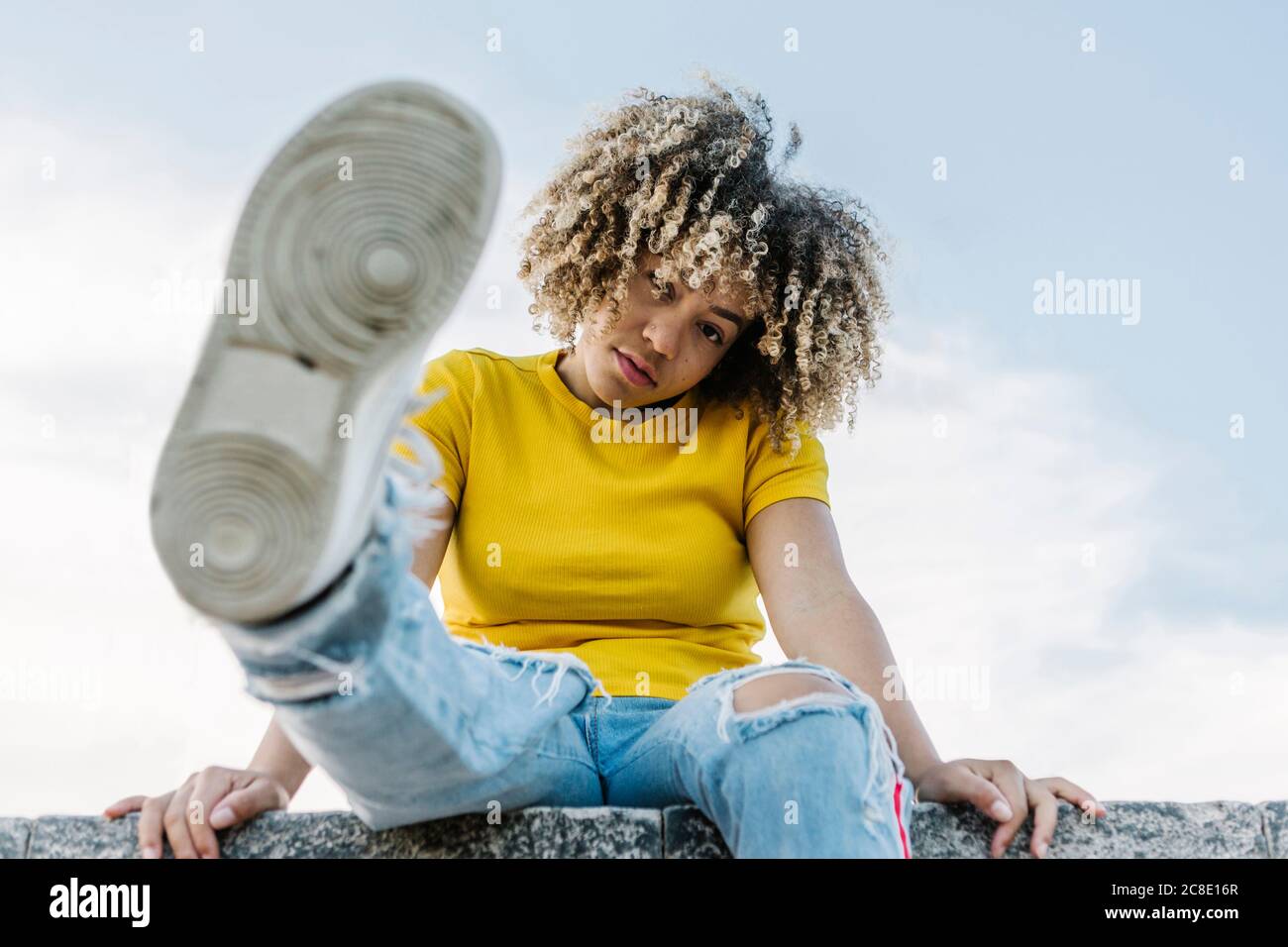 Young woman sitting on wall, showing sole of shoe Stock Photo - Alamy