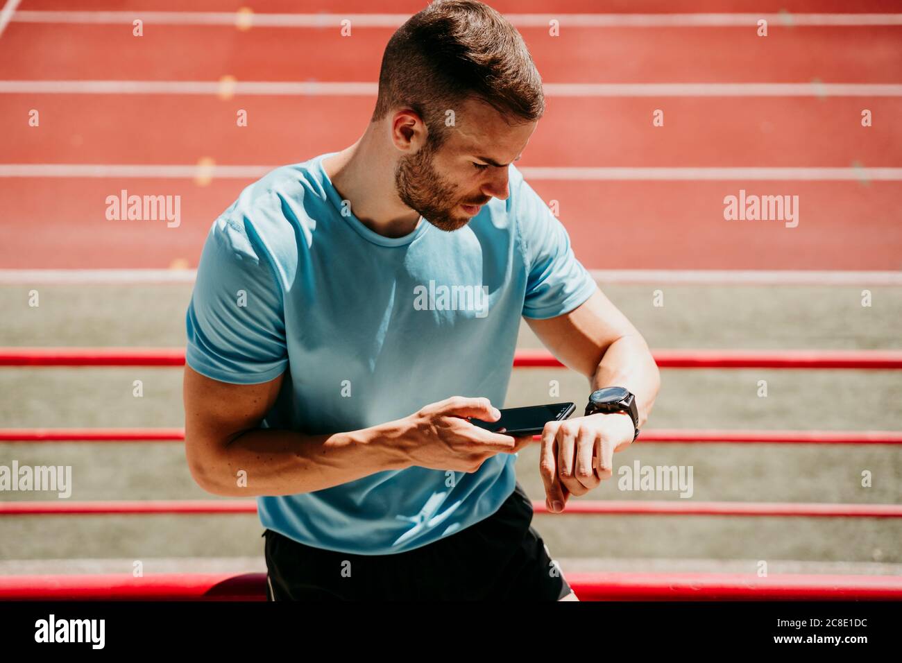 Male athlete in stadium checking smartwatch and smartphone Stock Photo ...
