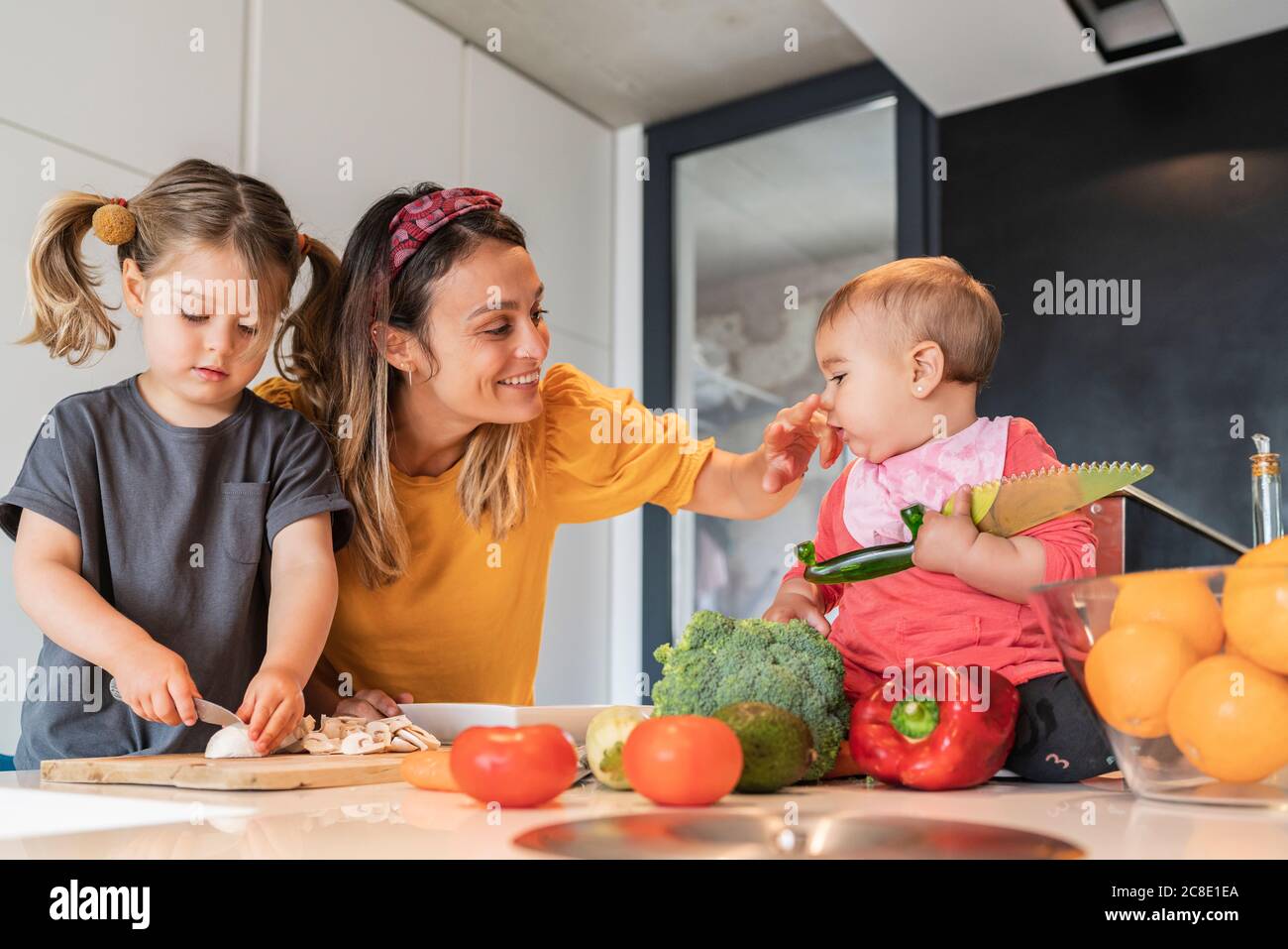 Mother playing with daughter while girl cutting vegetables on kitchen ...