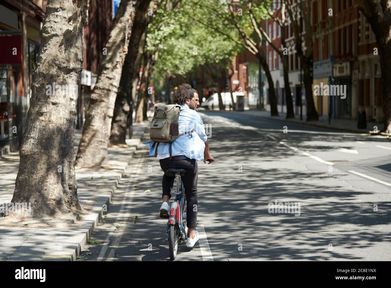 Back view of young man riding rental bike on bicycle lane, London, UK ...