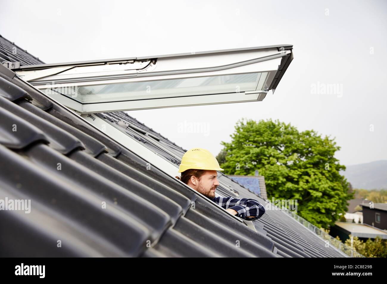 Man wearing hard hat looking out of roof window Stock Photo - Alamy