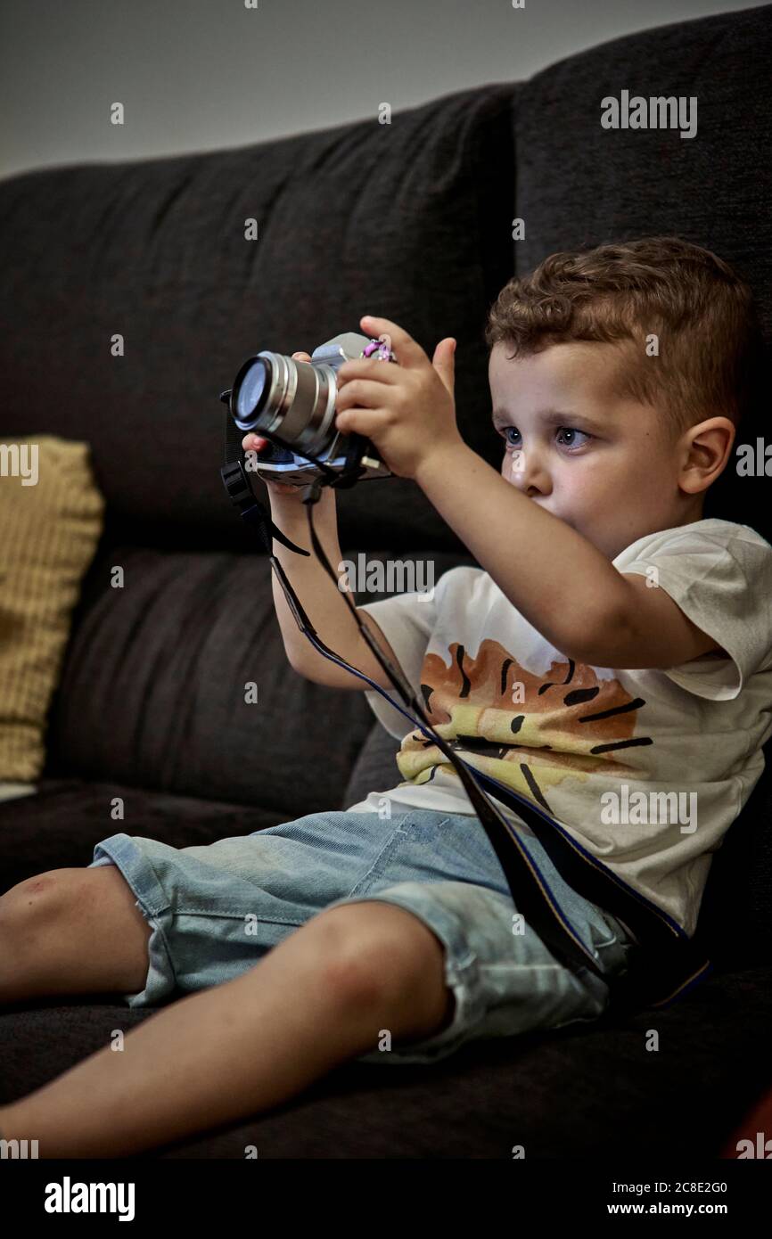 Cute boy photographing with camera while sitting on sofa at home Stock ...