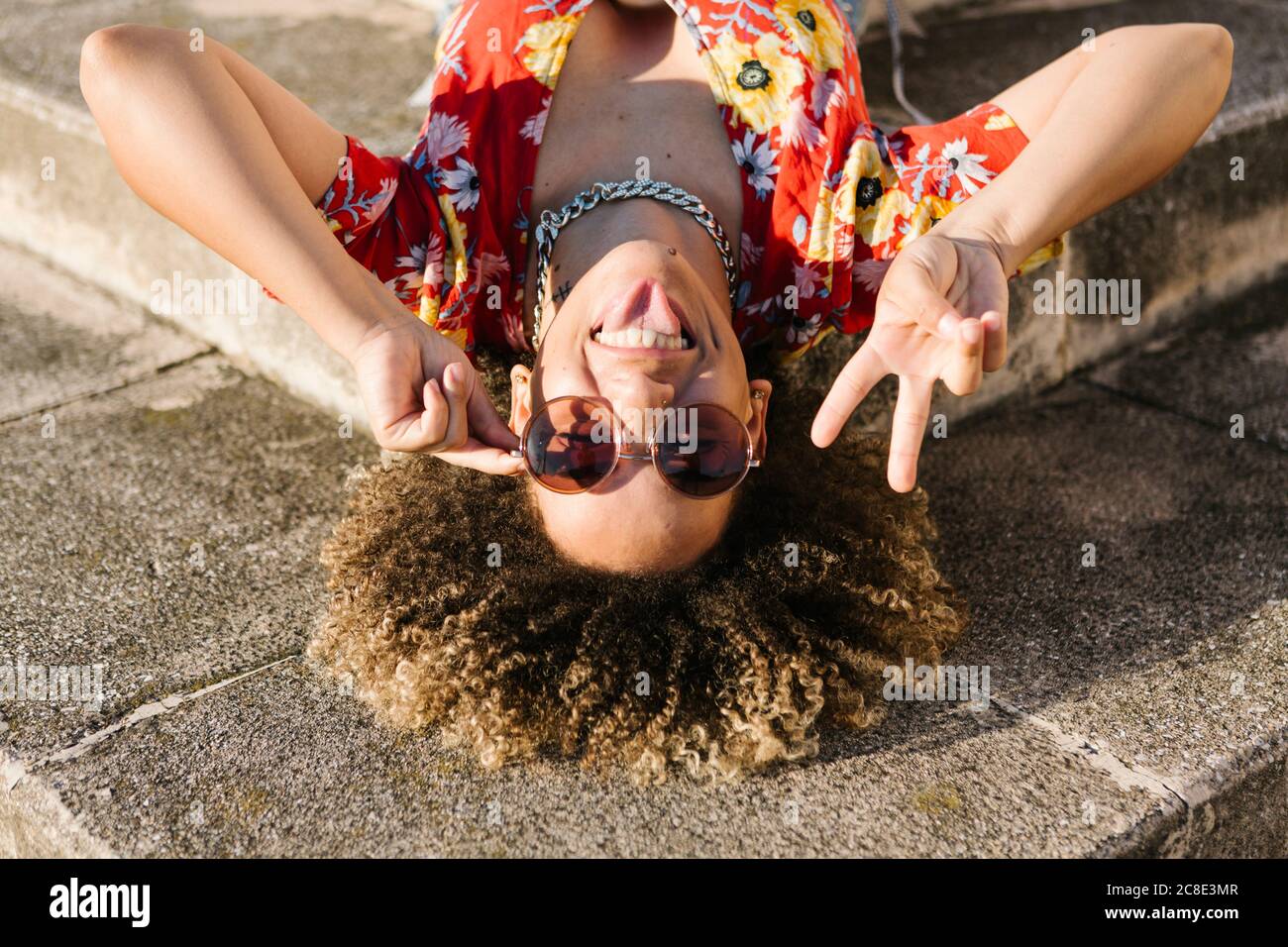 Trendy young woman sticking out tongue while showing peace sign on ...