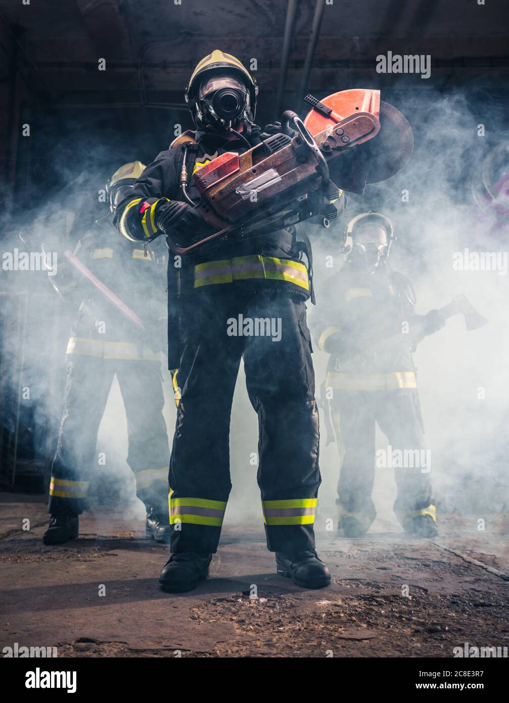 Portrait of fireman holding a rescue chainsaw in smoky garage of the ...
