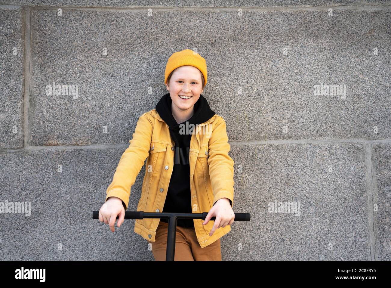 Happy boy holding push scooter while standing against wall Stock Photo ...