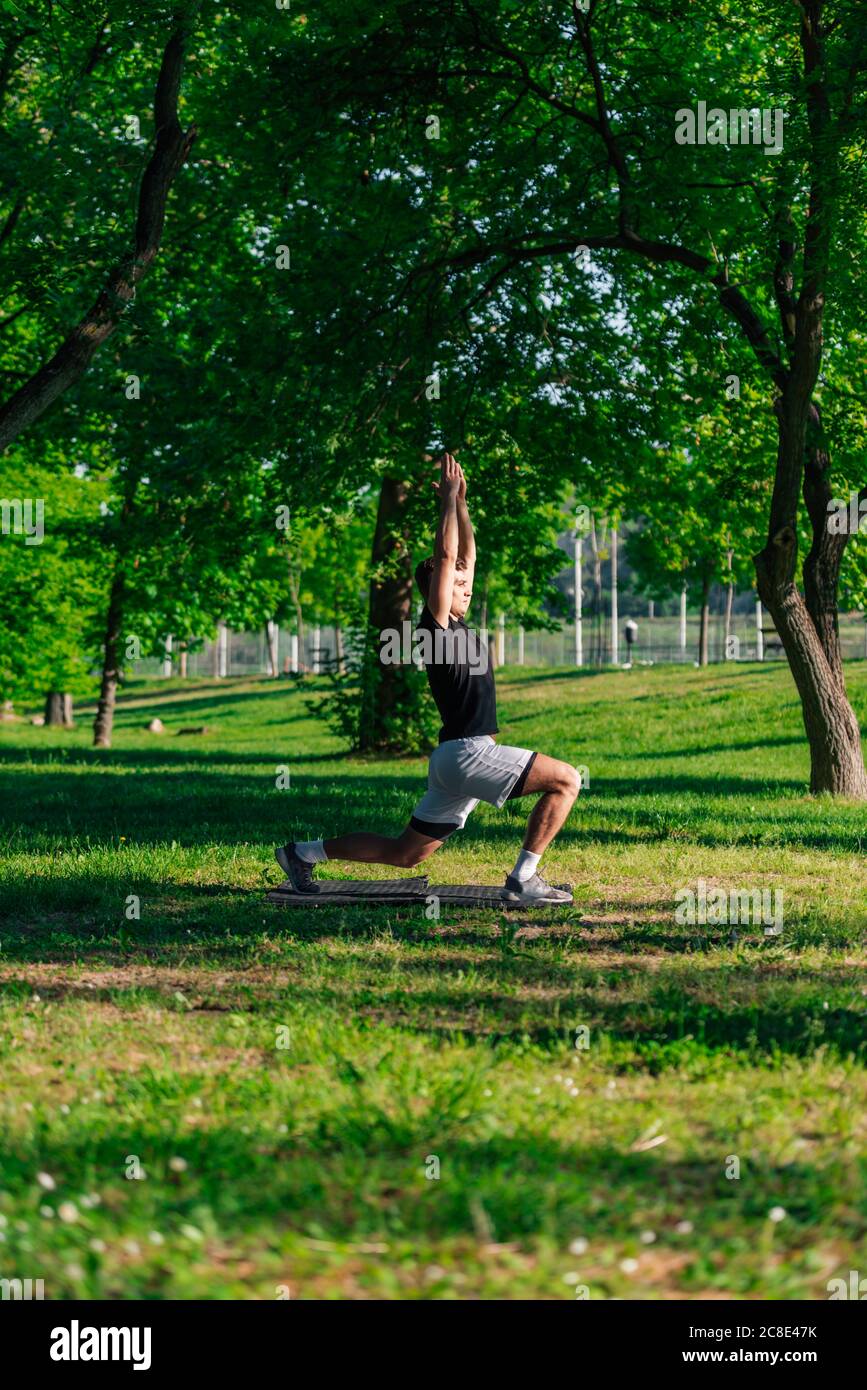 Sporty young man stretching legs and doing forward lunge while having ...