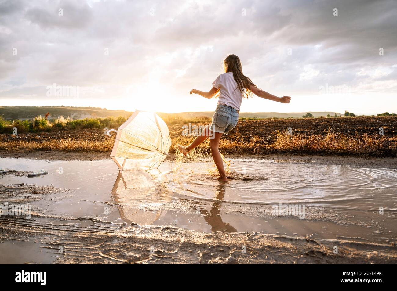 Girl splashing water over umbrella on puddle during sunset Stock Photo ...