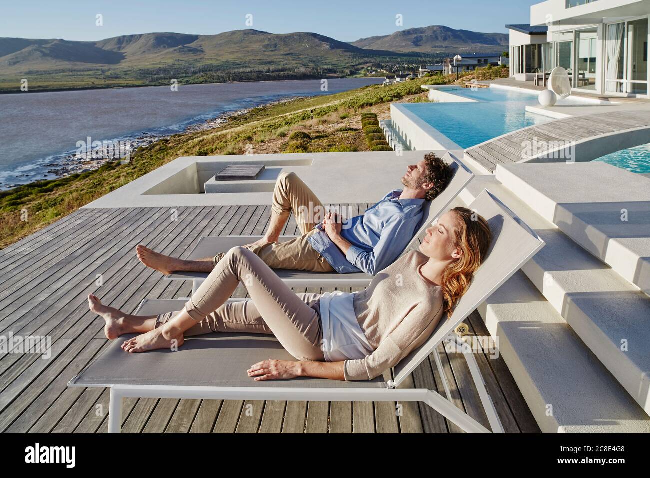 Couple lying on deck chairs at luxury beach house Stock Photo - Alamy