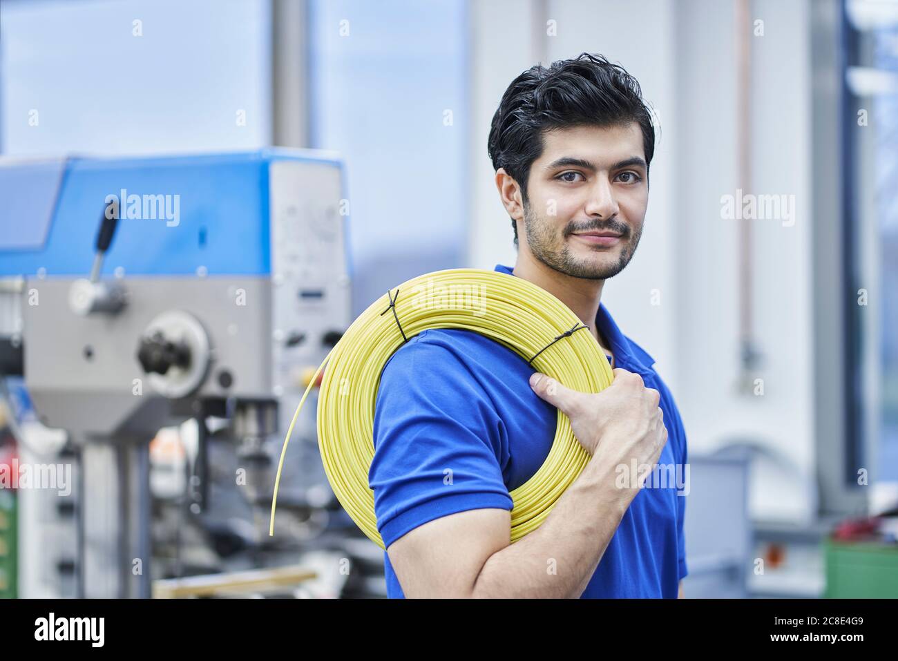 Confident male worker carrying rolled up cables in factory Stock Photo ...