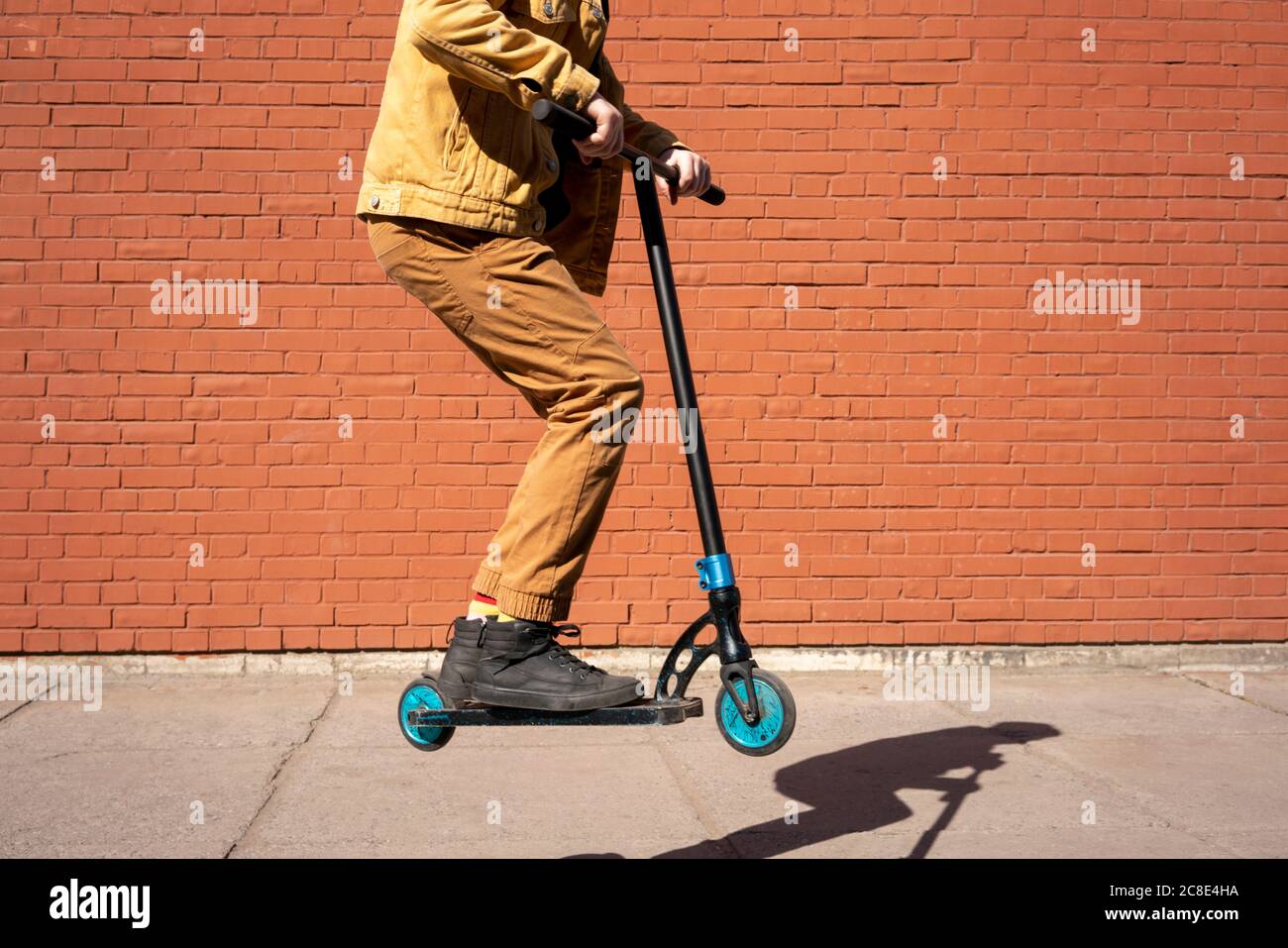 Boy performing stunt on with push scooter at sidewalk against brick ...