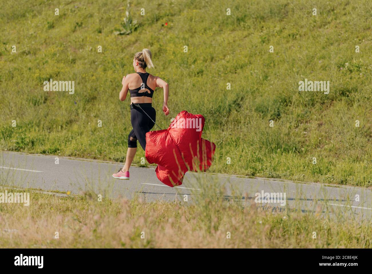 Side view of a young fitness woman running using red resistance ...