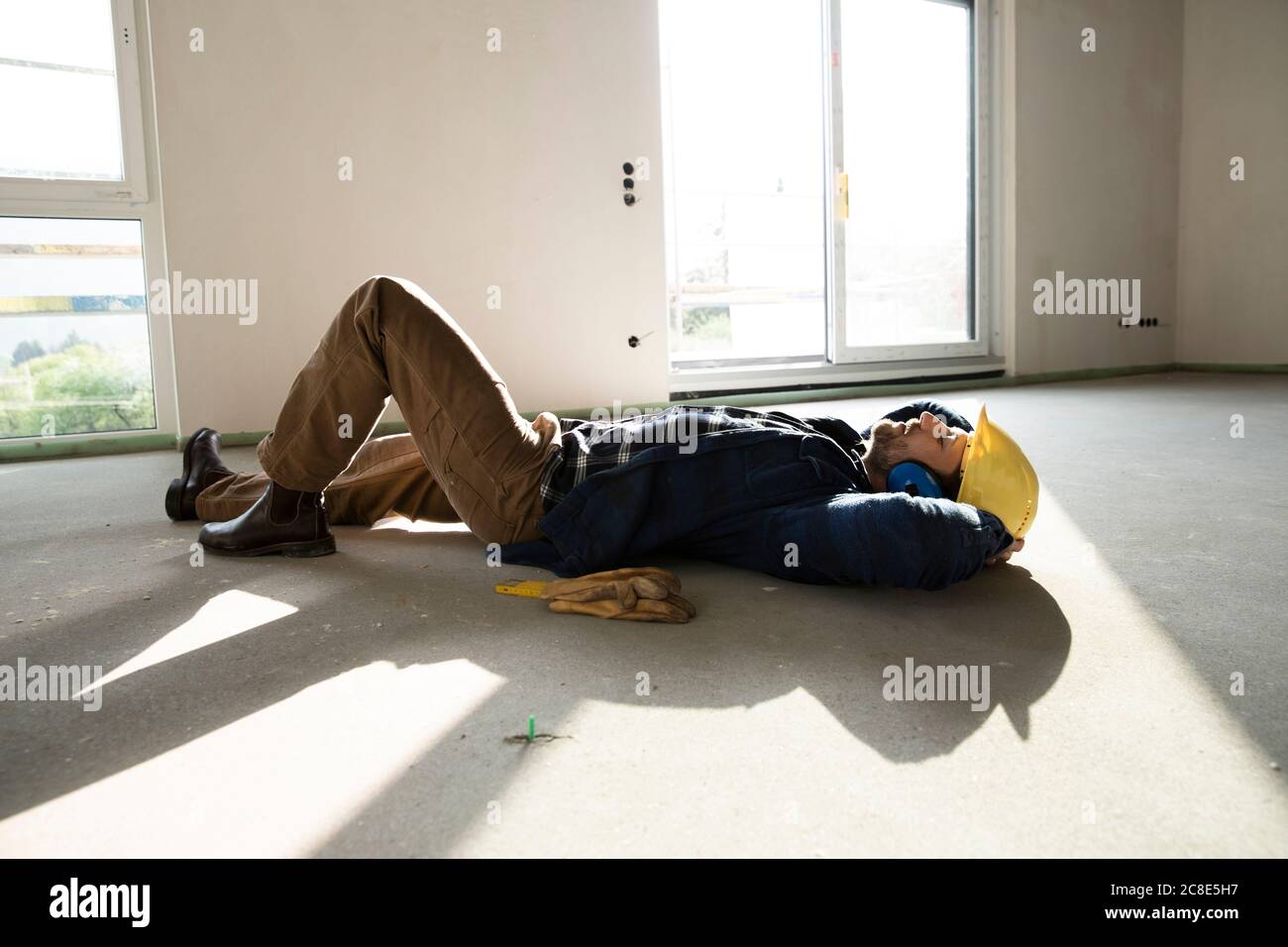 Construction worker with hands behind head sleeping on floor in house ...