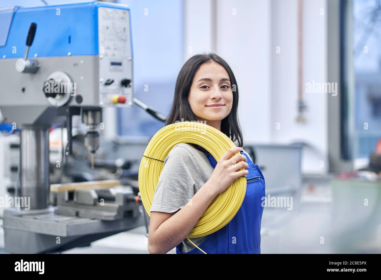 Happy female worker carrying rolled up cables in factory Stock Photo ...