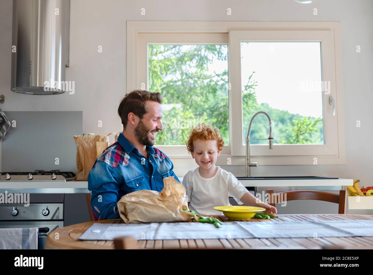 Happy father and son enjoying while sitting at dining table with green ...