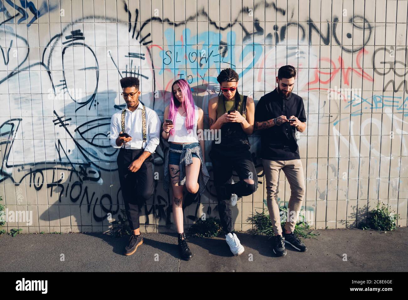Group of friends using smartphones at a graffiti wall in the city Stock ...