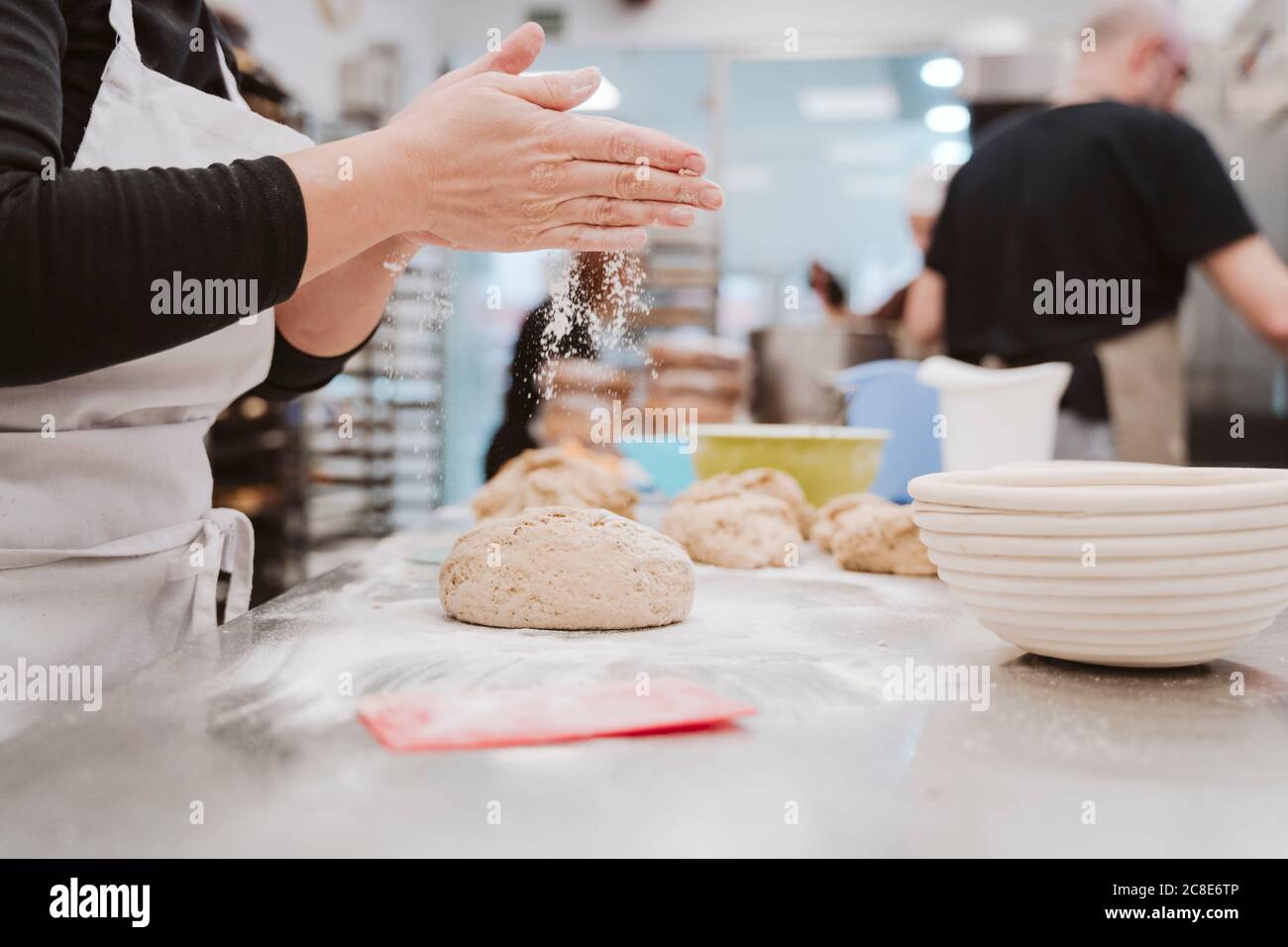 Female baker sprinkling flour on bread dough on kitchen counter in ...