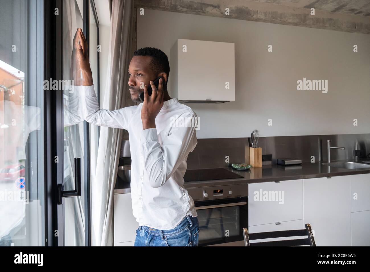 Portrait of pensive man on the phone at home looking out of window ...