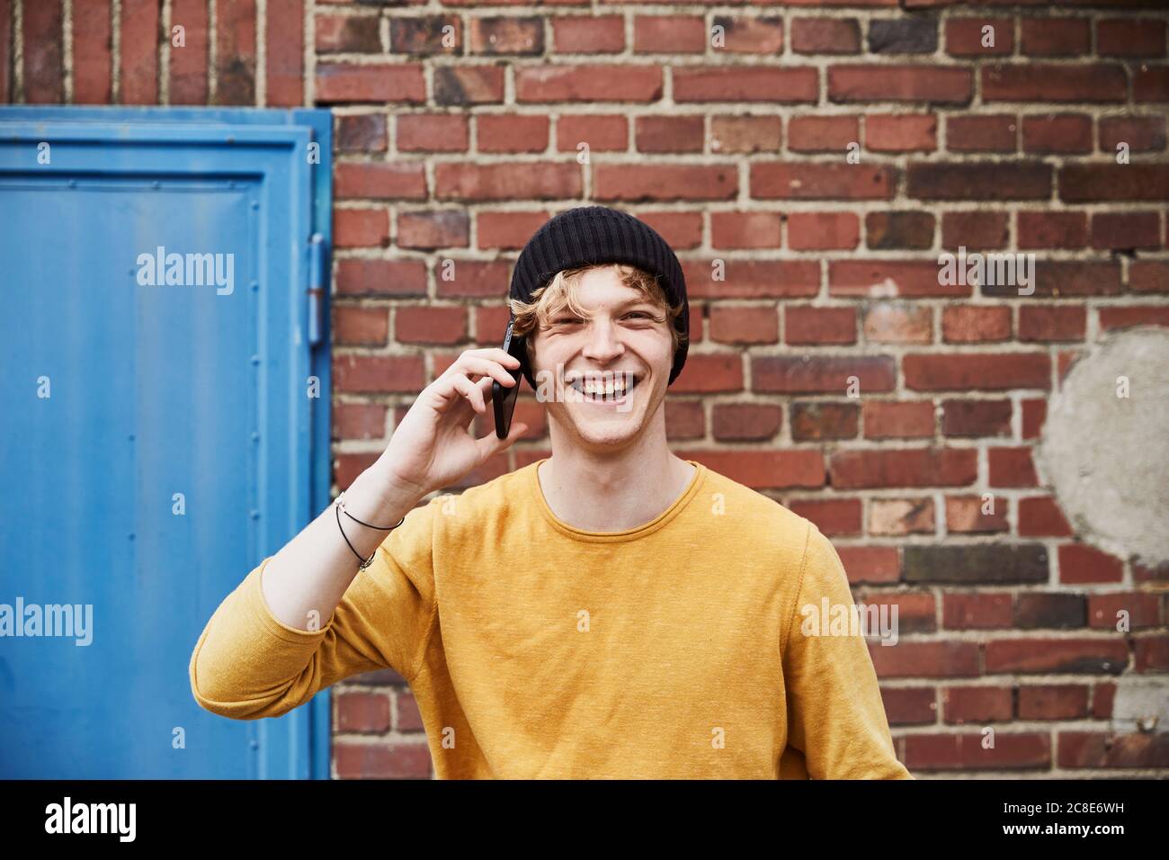Portrait of laughing young man on the phone in front of brick wall ...