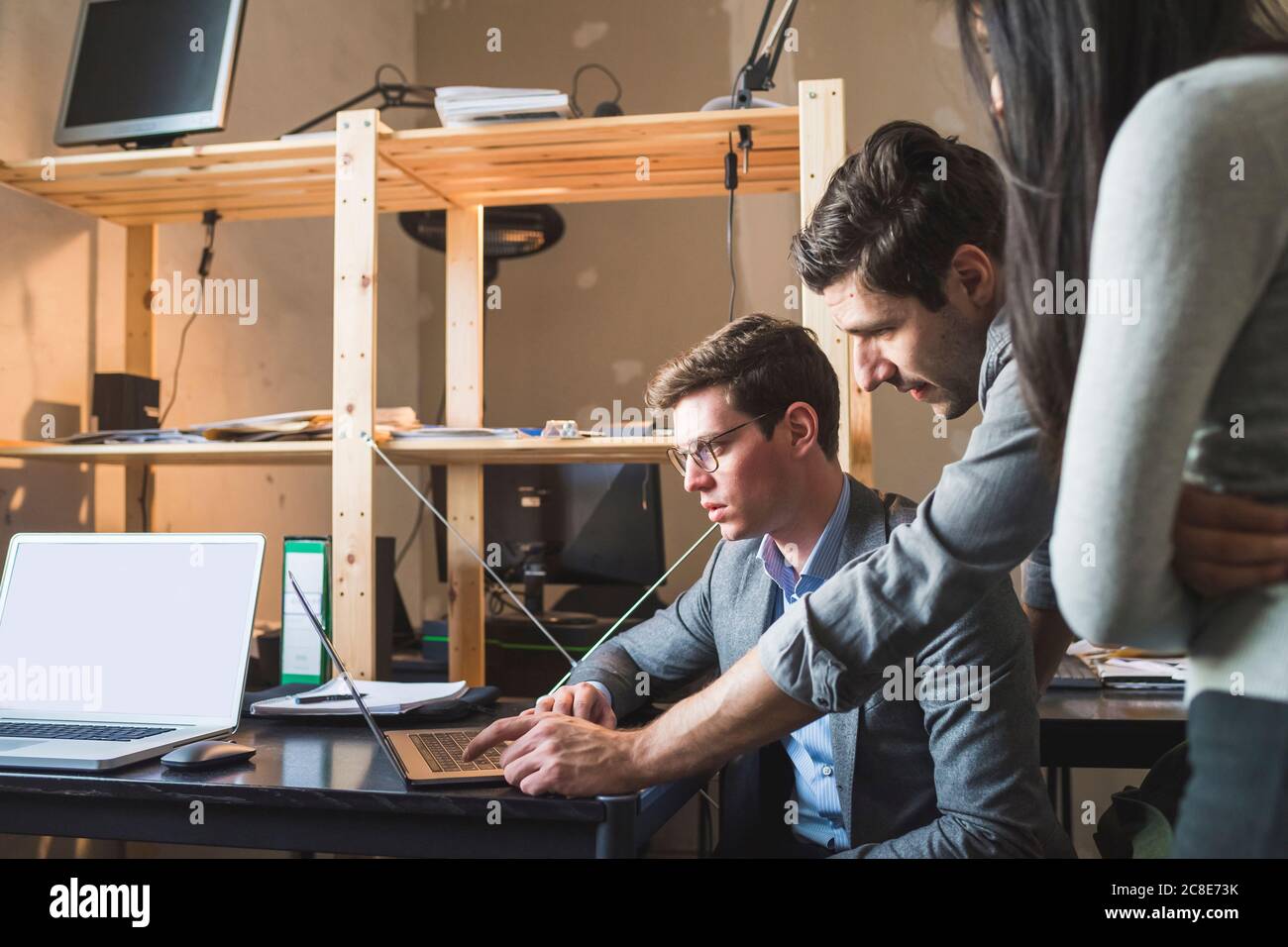 Three business people sharing laptop at desk in office Stock Photo - Alamy