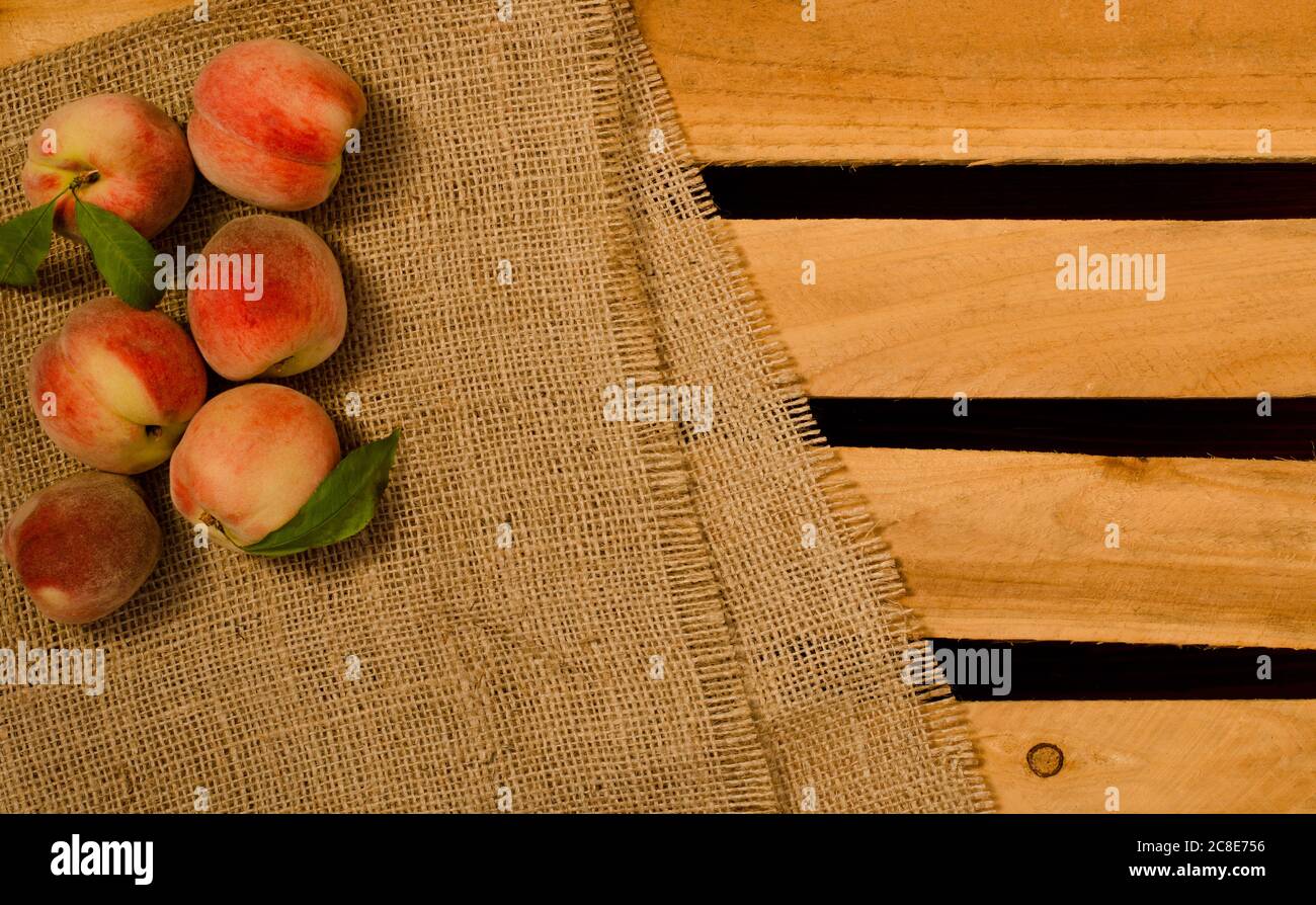Six ripe peaches with leaves on sackcloth and wooden plates, place for ...