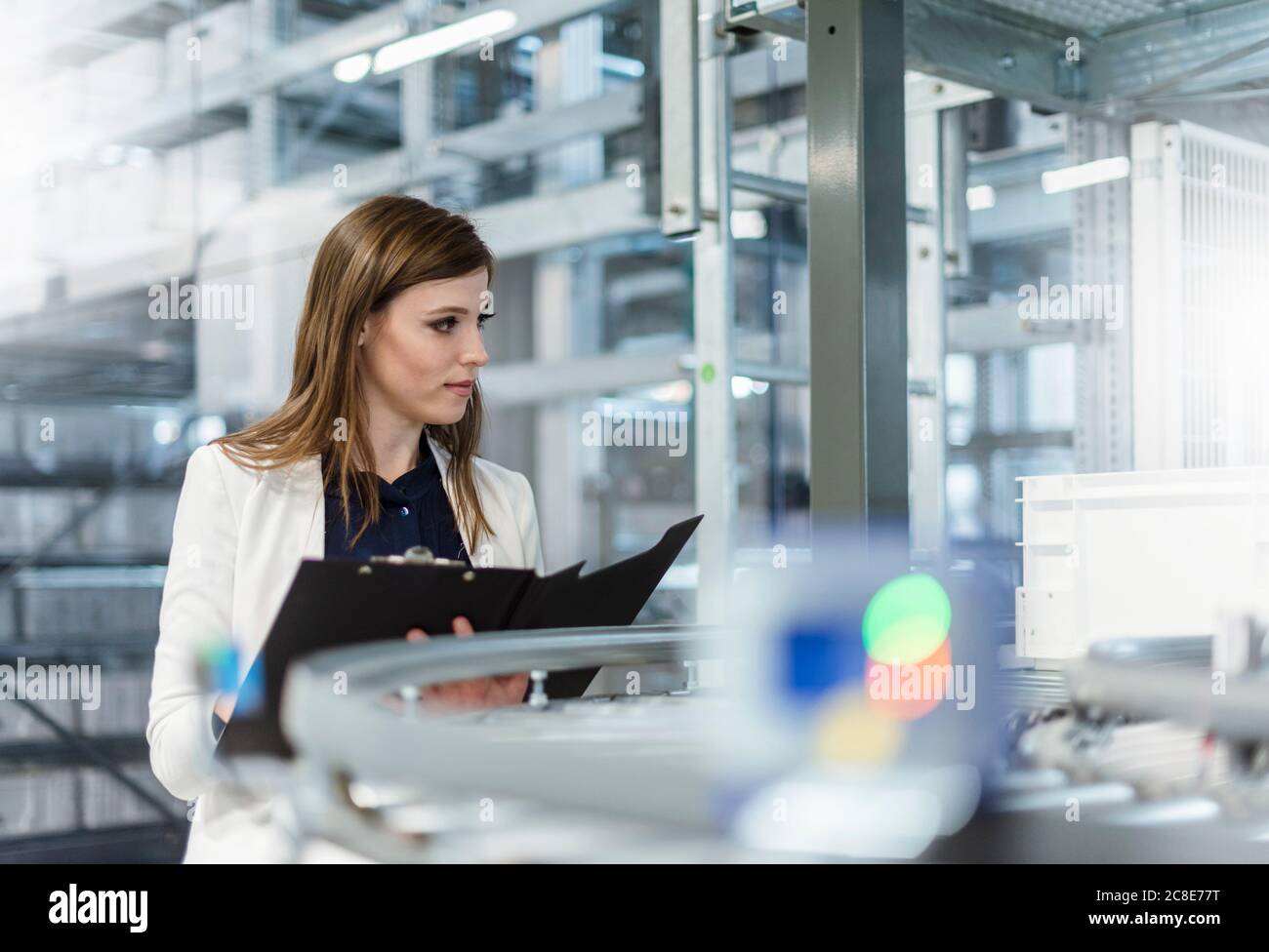 Female manager holding file while examining production line in factory ...