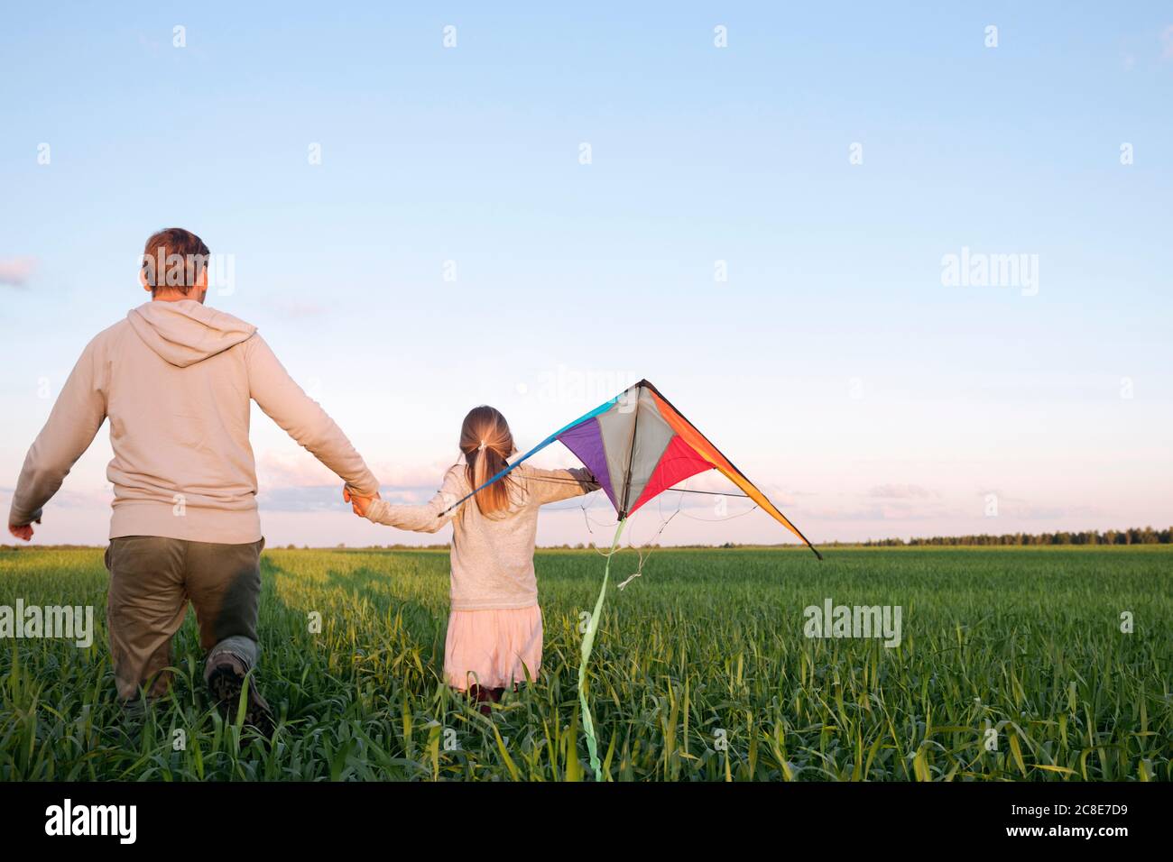 Girl holding kite walking with father amidst plants on green landscape ...