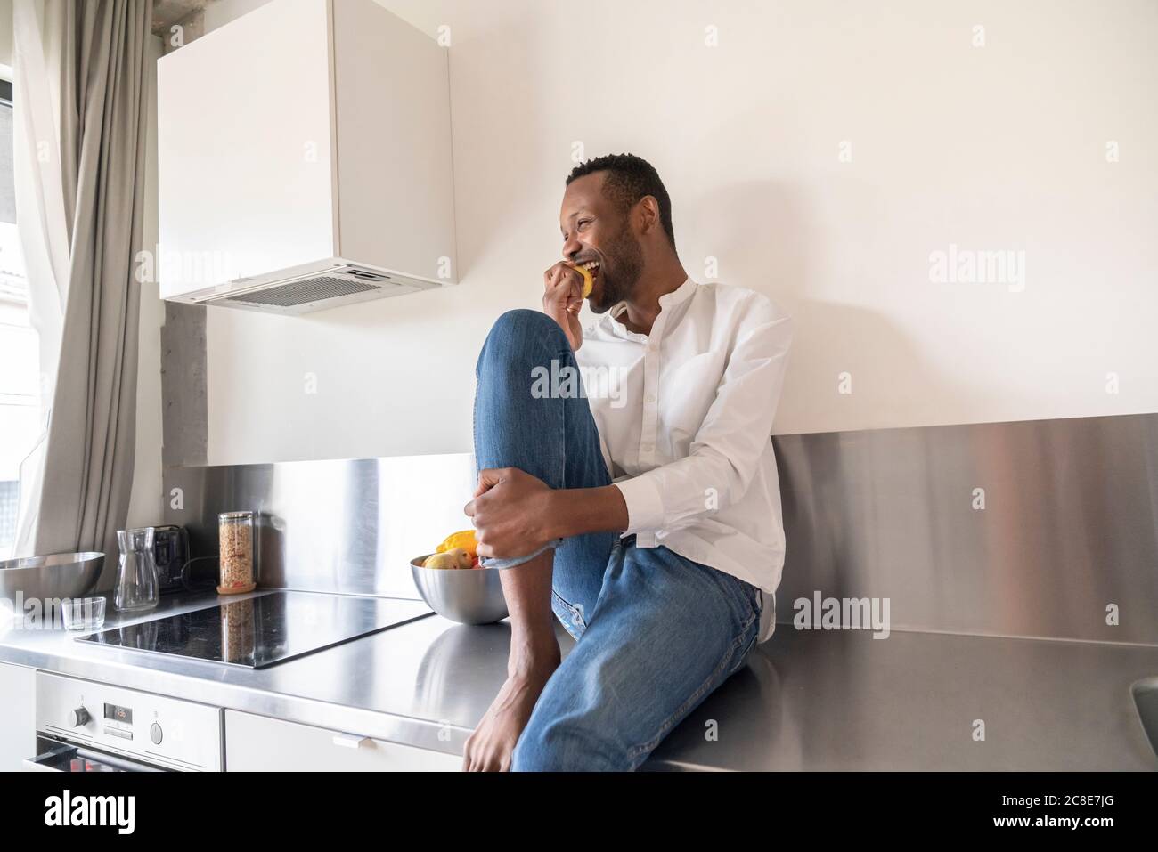 Laughing man sitting on kitchen counter at home eating an apple Stock ...