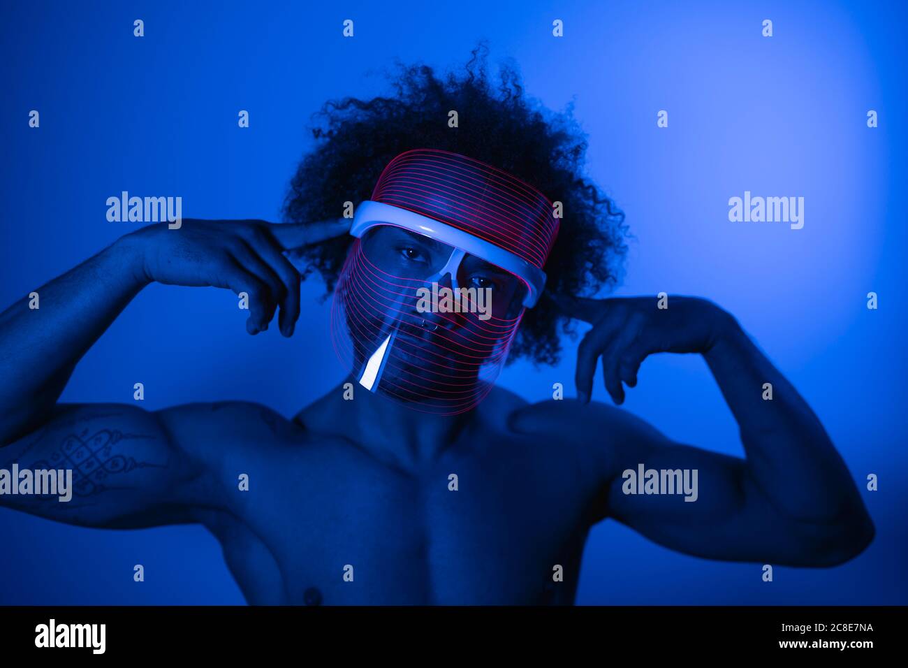 Shirtless young man wearing red led mask against wall at home Stock ...