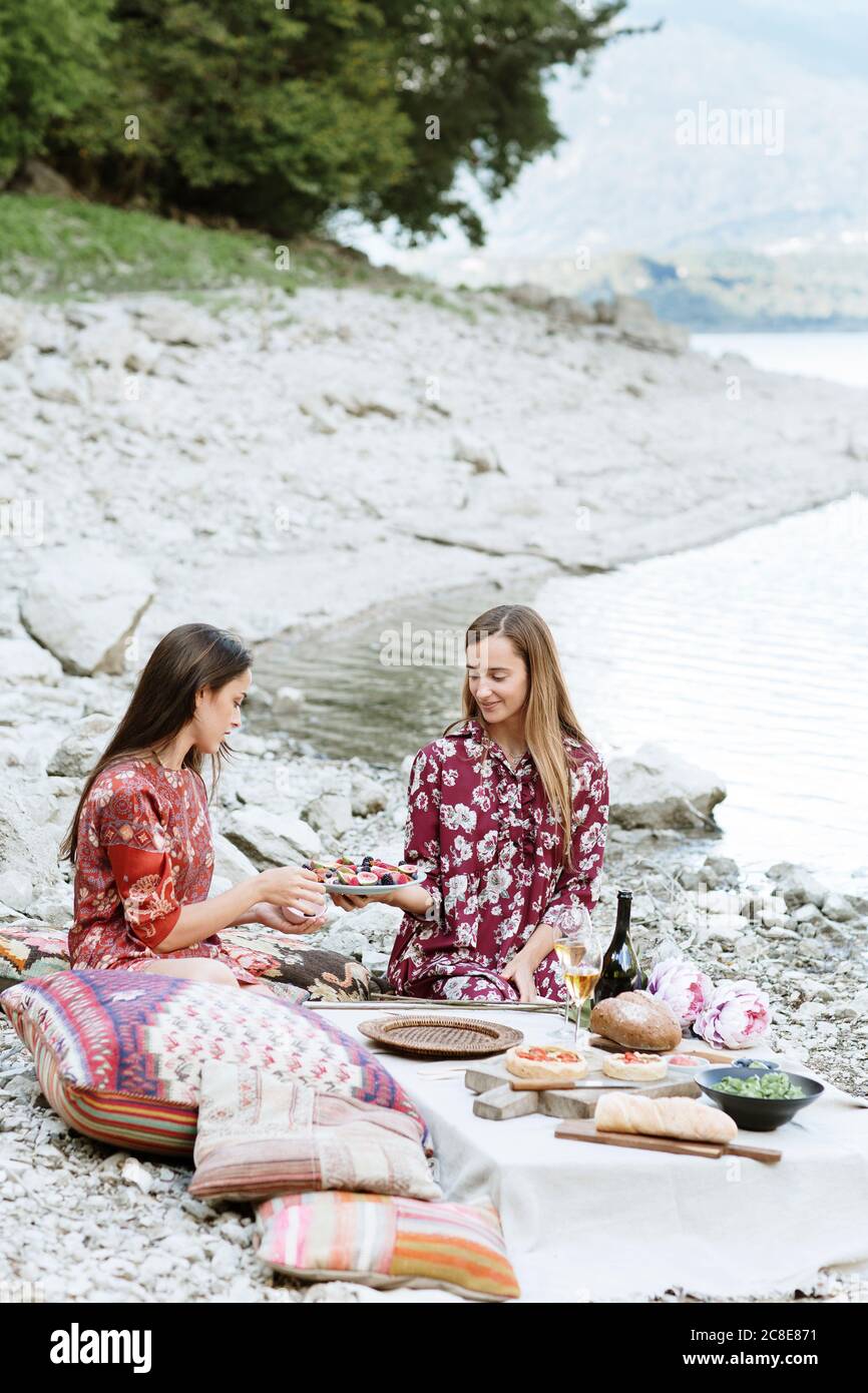 Woman offering fruit salad to female friend while enjoying picnic at ...