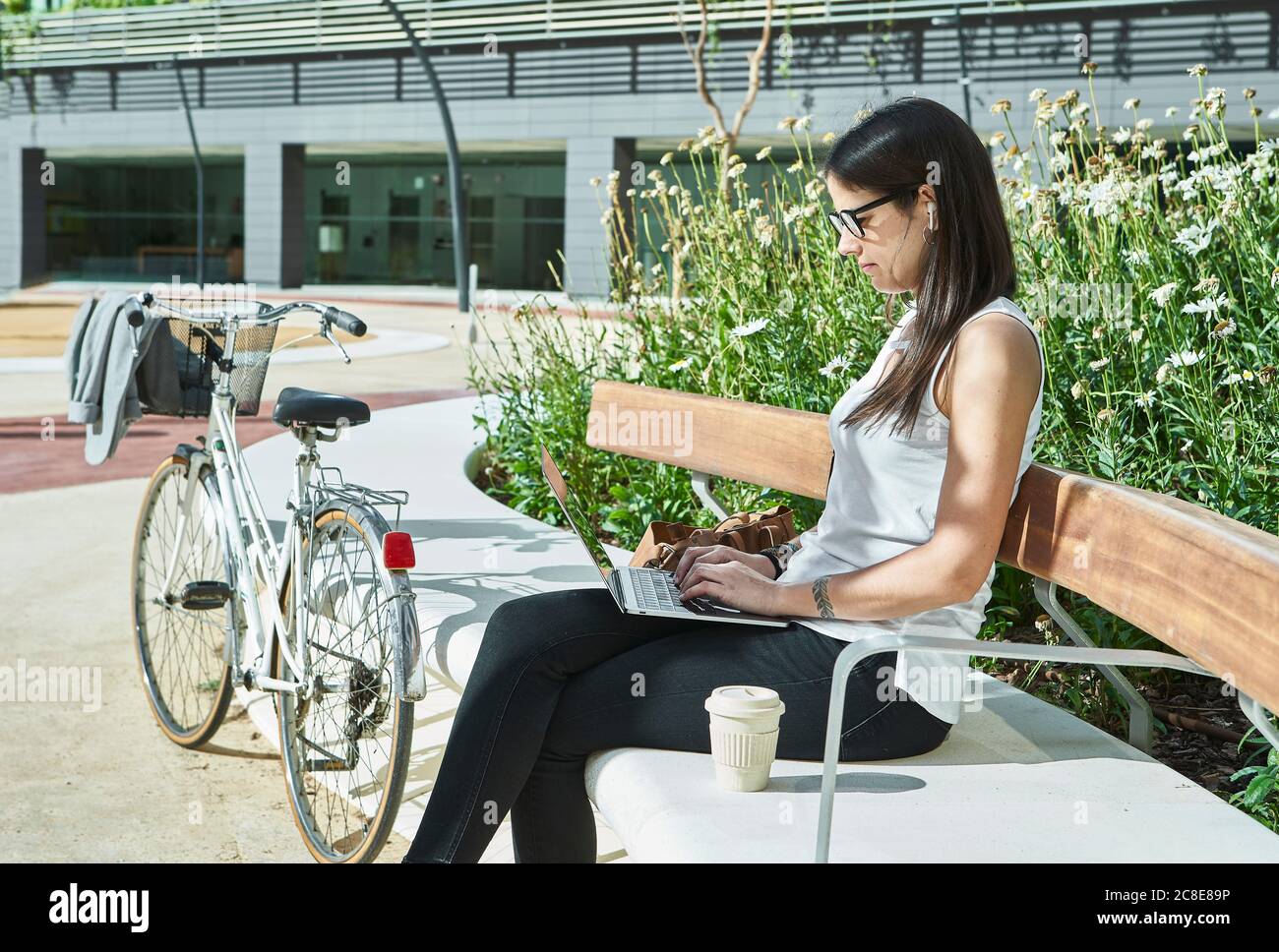 Female commuter using laptop while sitting on bench in city during ...