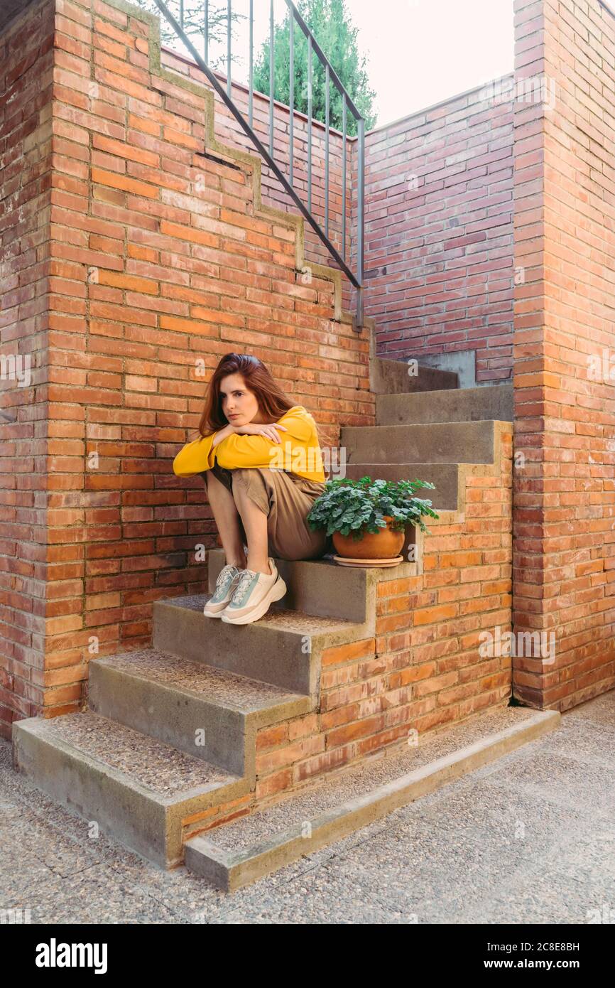 Sad thoughtful young woman sitting on steps by brick wall Stock Photo ...